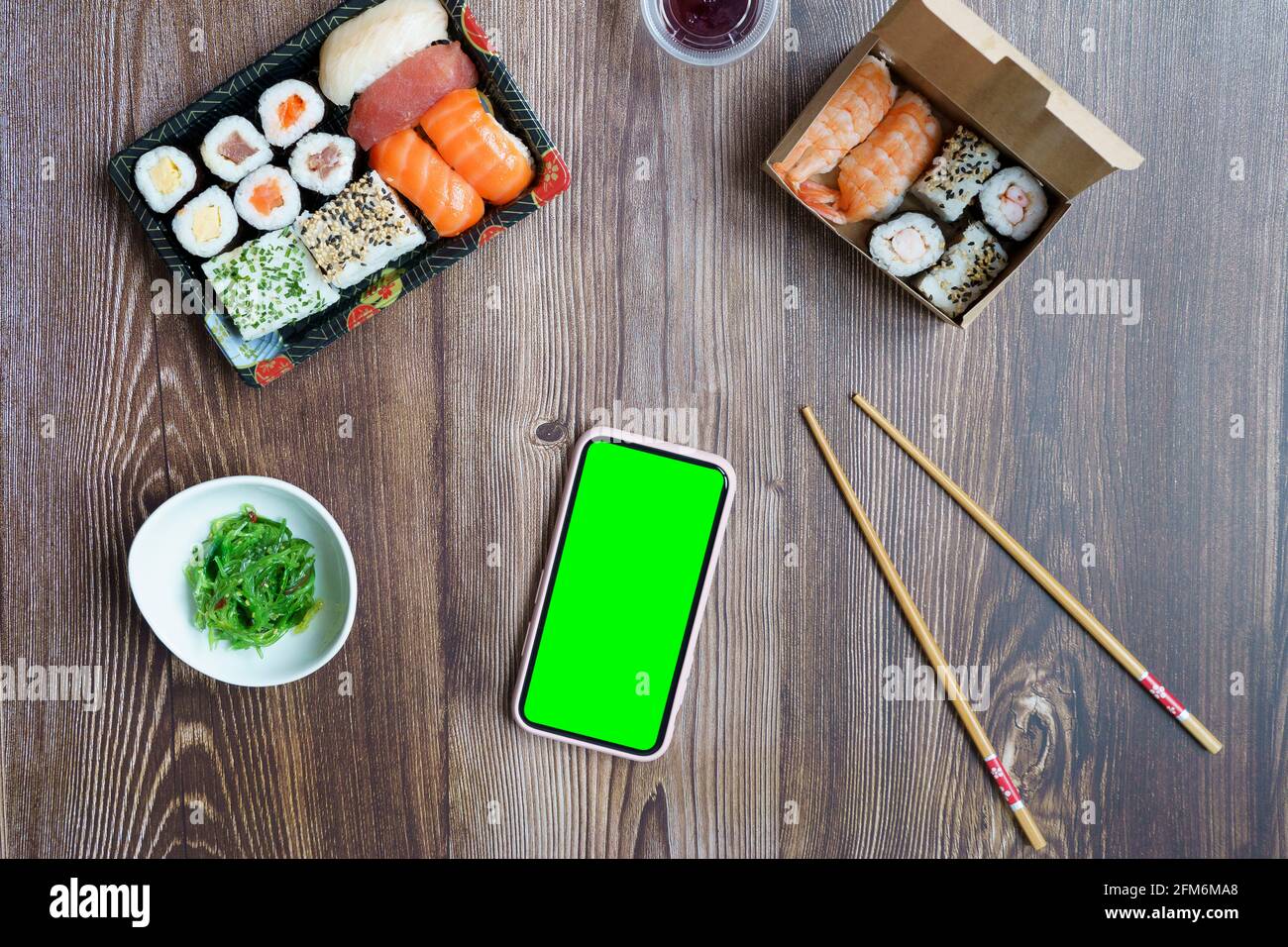 Phone with green screen on a wooden table with sushi food in take-away ...