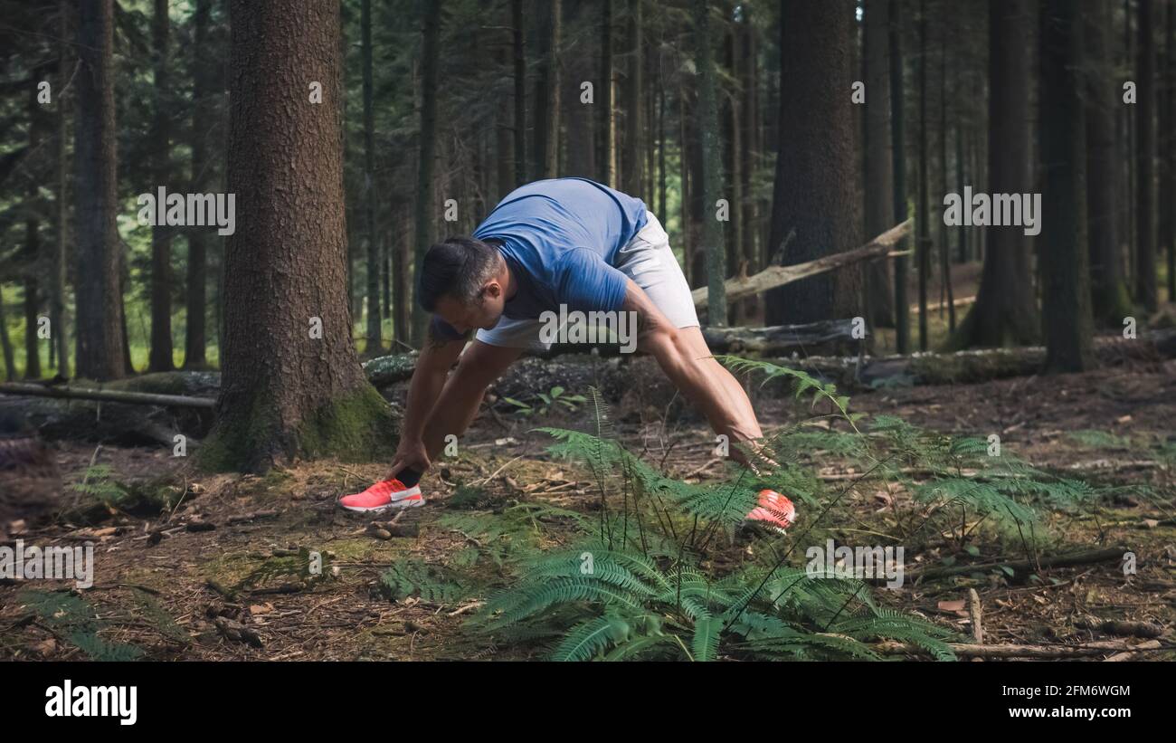 Wide shot of Caucasian man in sportswear doing legs and back stretching ...