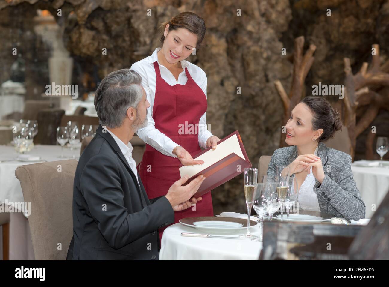 young waitress suggesting menu to couple in restaurant Stock Photo - Alamy