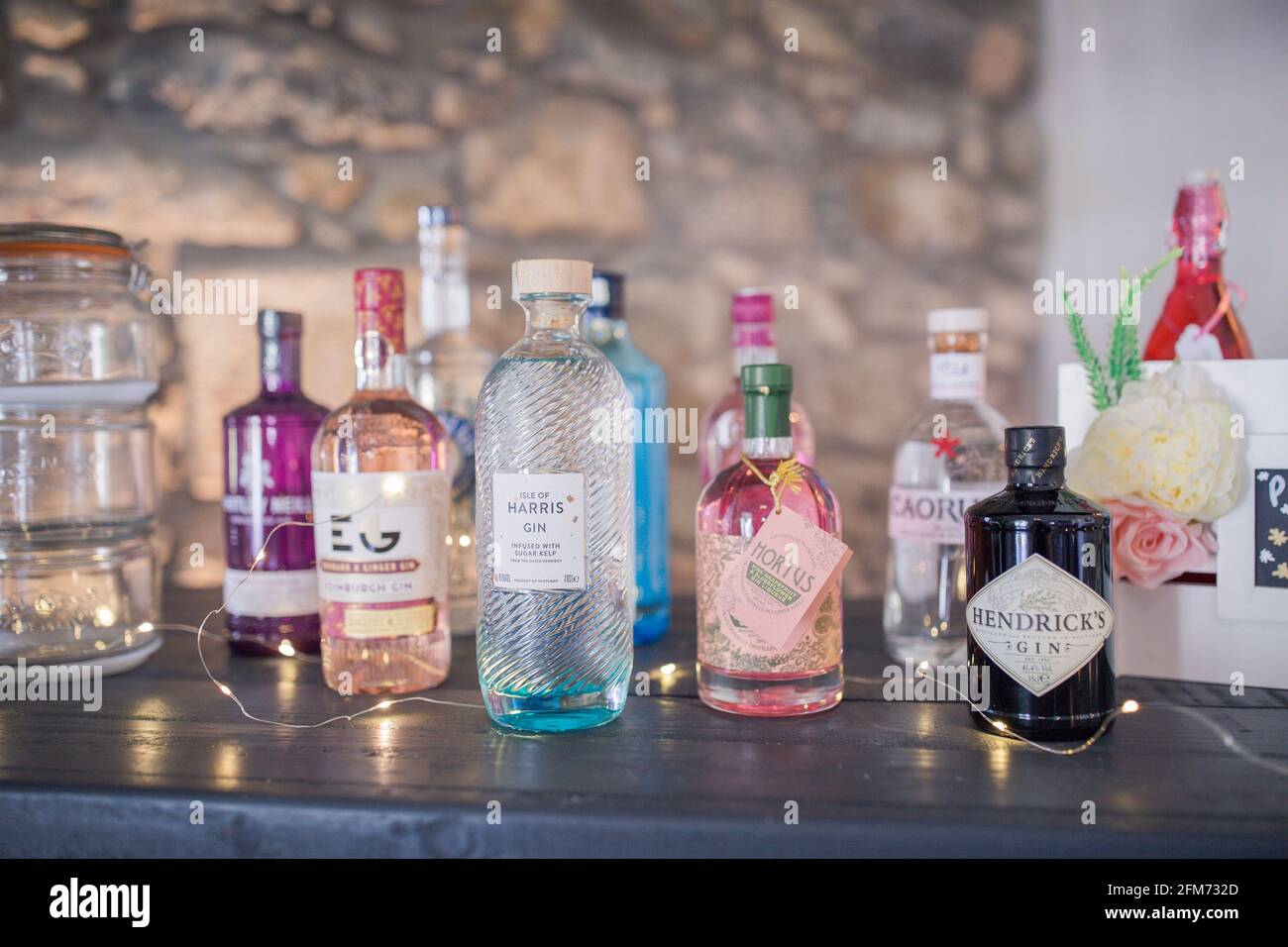 Colourful bottles of gin set out on a black table or bar with a stone ...