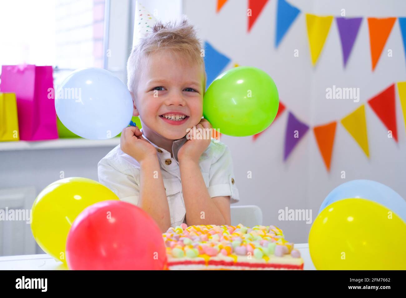 Excited Birthday boy with colorful balloons near birthday rainbow cake ...