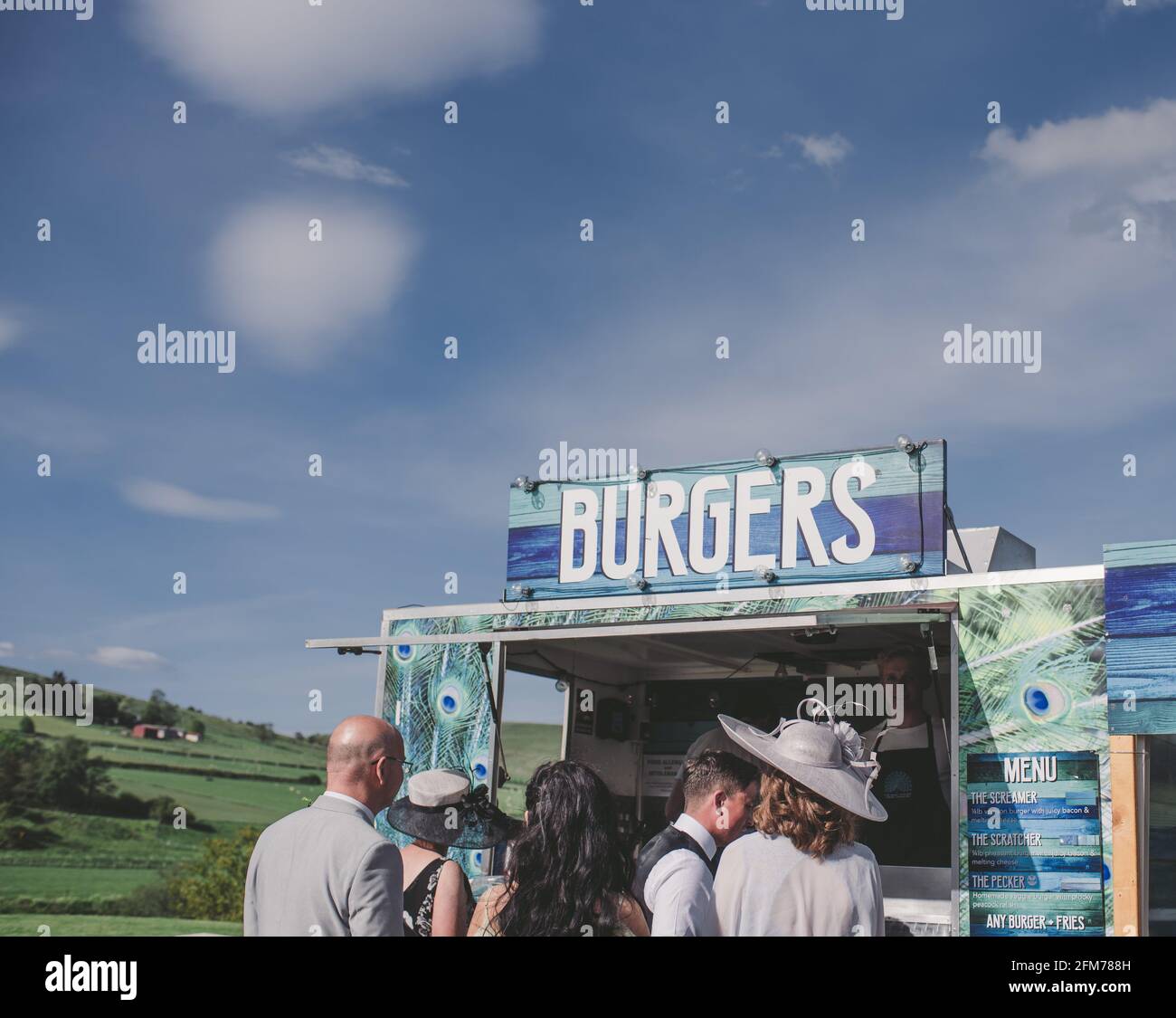 guests at a wedding queue at outside burger catering van in summer ...