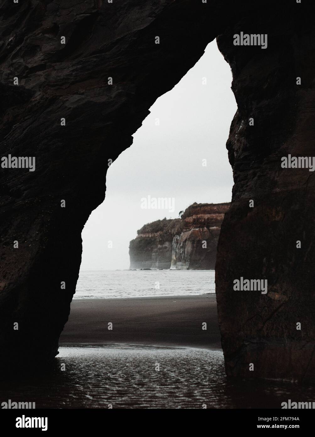 Vertical shot of a coast and cliff captured through the natural arch ...
