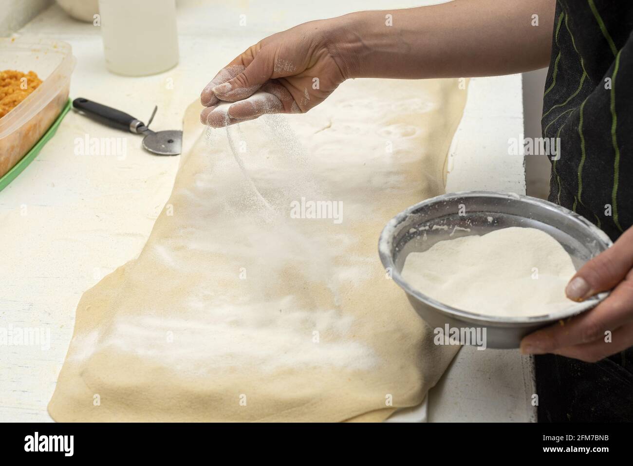 Person scattering flour on the dough in the process of preparation of ...