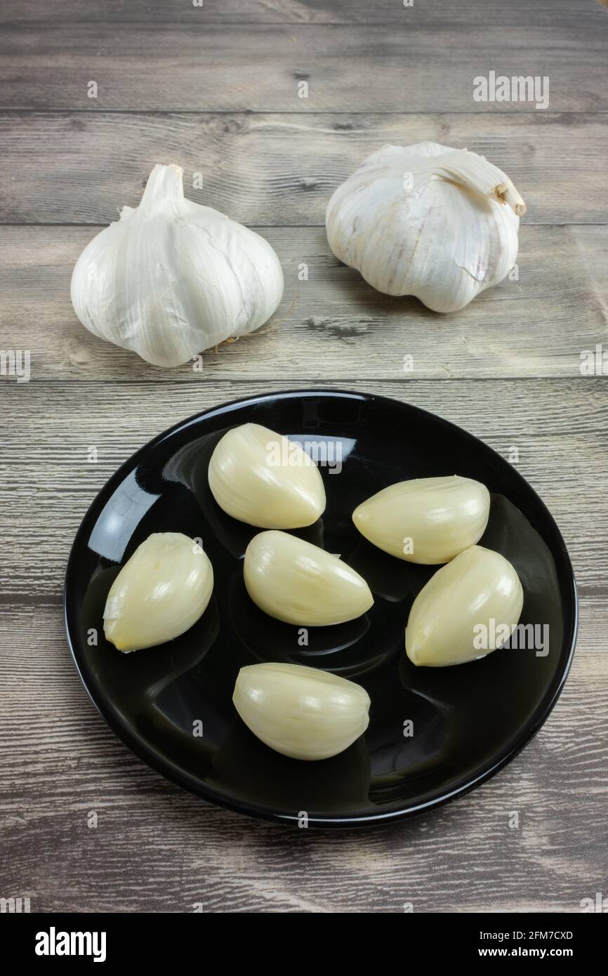 Two gloves of garlic and peeled heads of garlic on the black plate ...