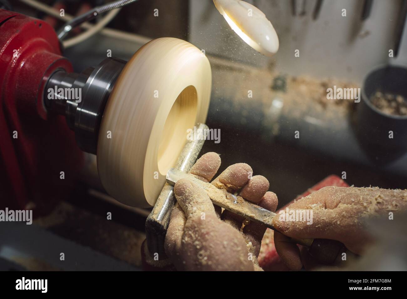 Joinery worker shaping a piece of wood on the lathe with wood shavings ...