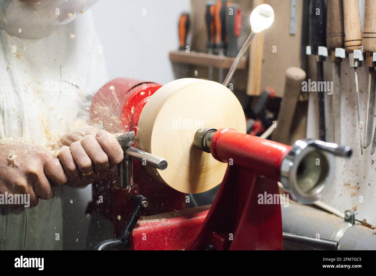 Closeup of a woodworker shaping a piece of wood on the late with small ...