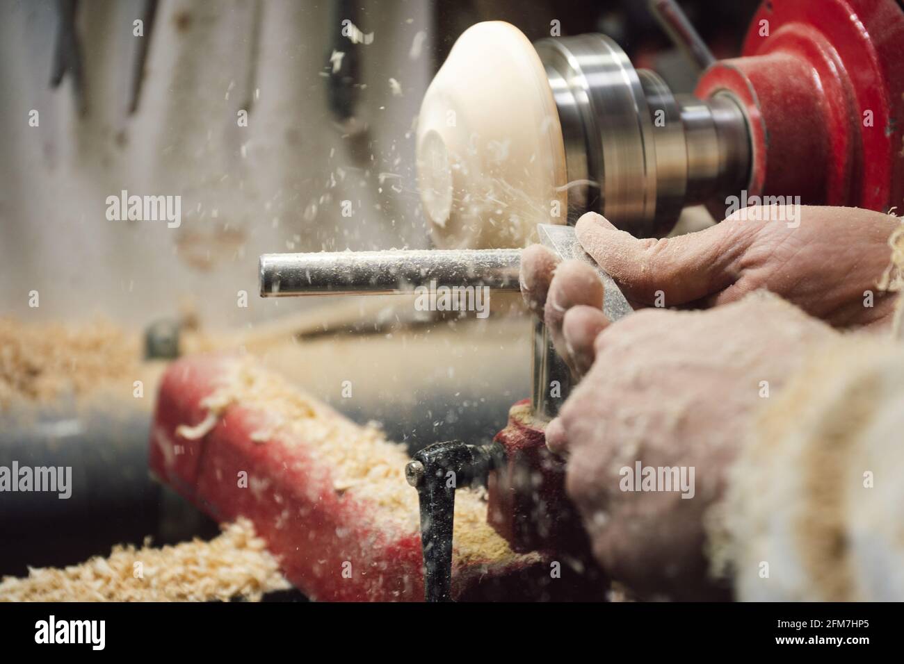 Closeup of a woodworker shaping a piece of wood on the lathe with dust ...