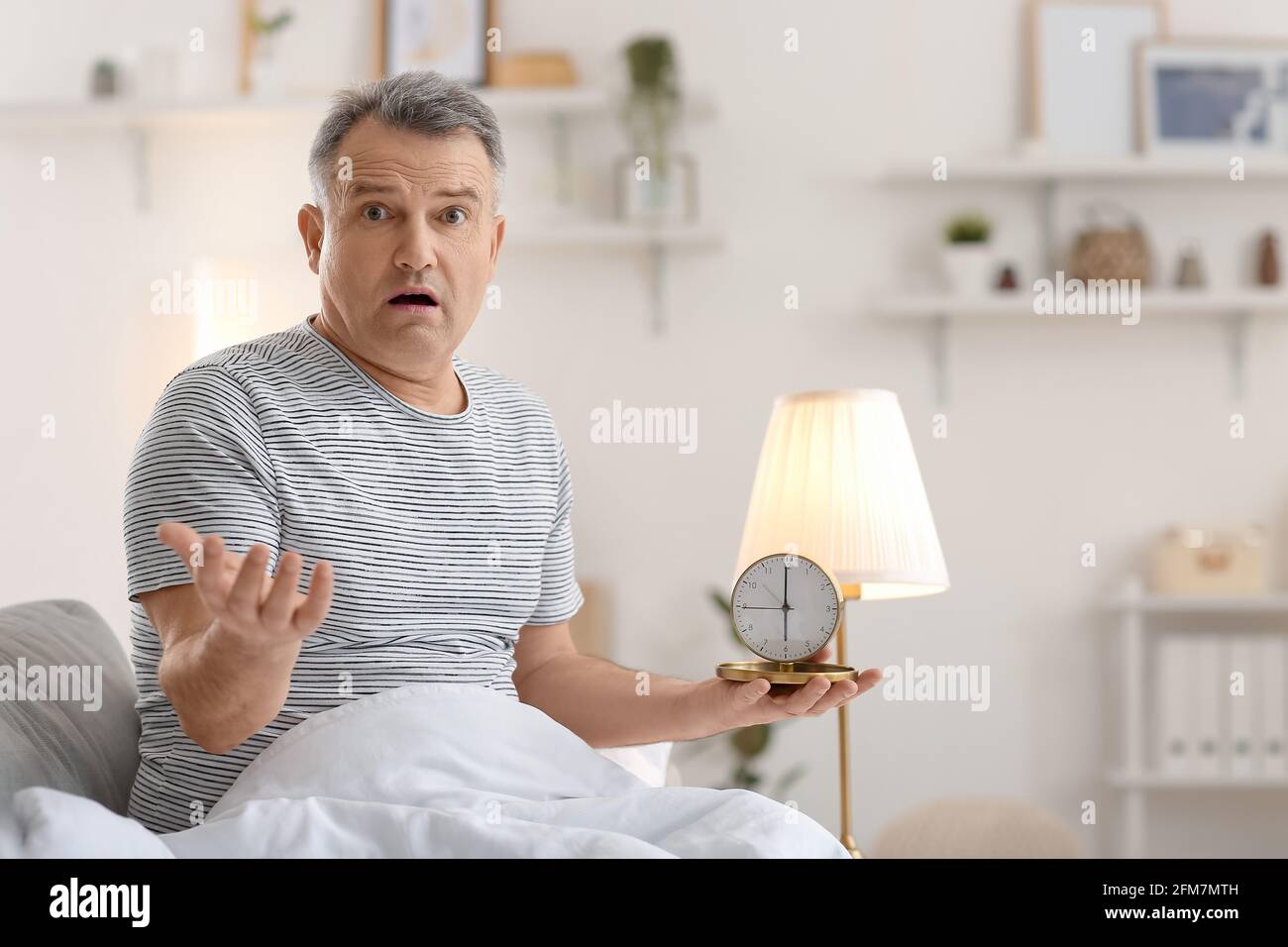 Confused mature man with alarm clock in bedroom Stock Photo - Alamy