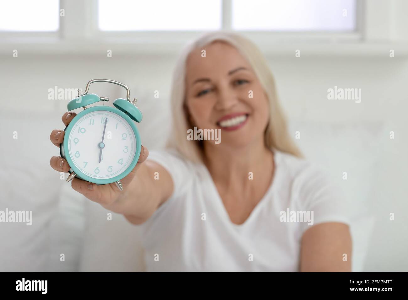 Mature woman with alarm clock in bedroom Stock Photo - Alamy
