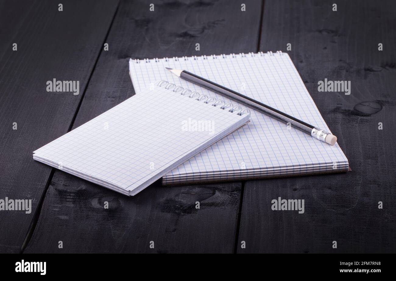 Pencil and notepad with spiral on black wooden textured table. Side ...