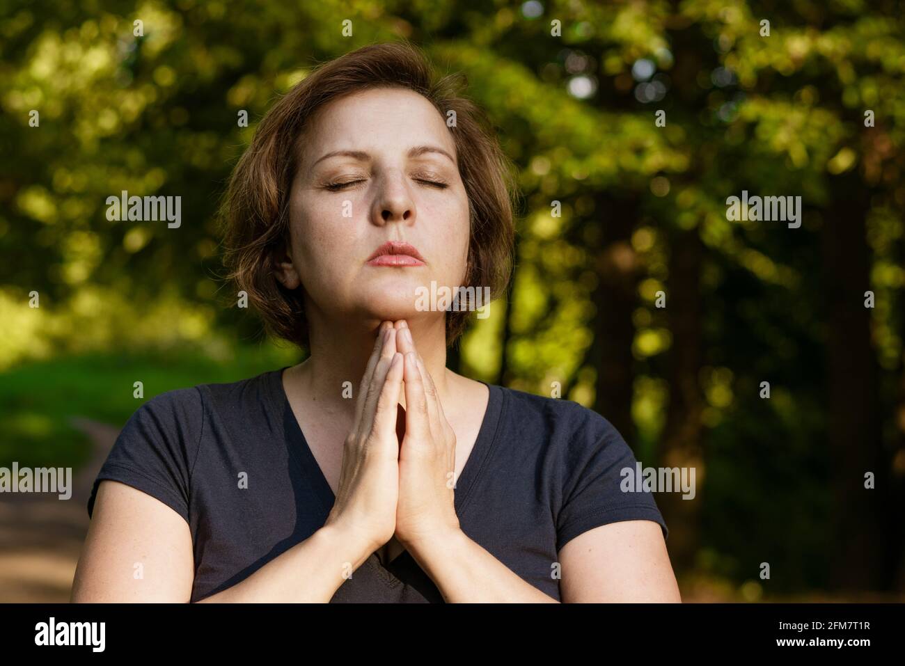 adult woman with short hair meditates with folded palms in the park ...
