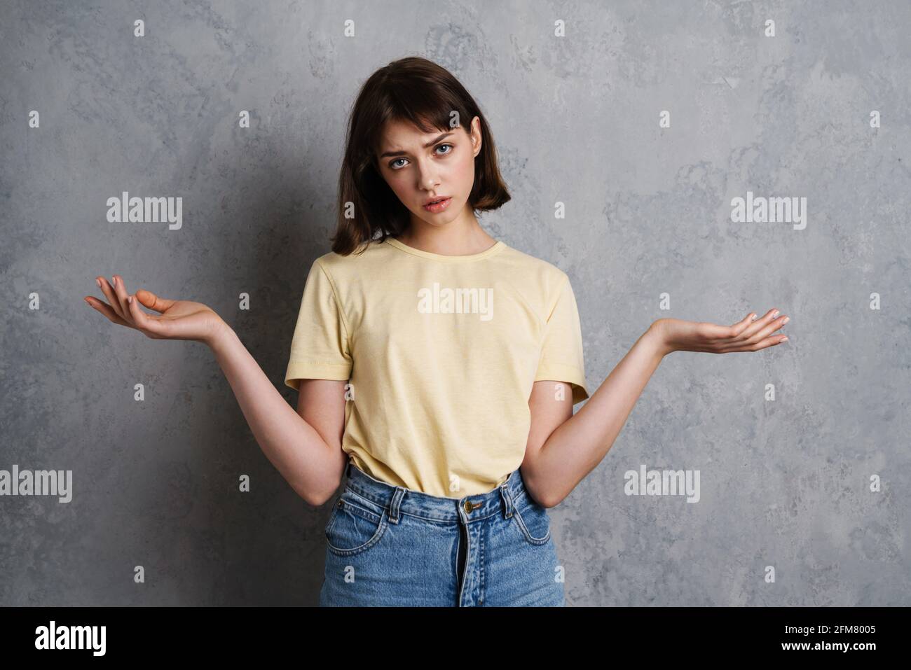 Confused young girl shrugging shoulders while standing isolated over ...