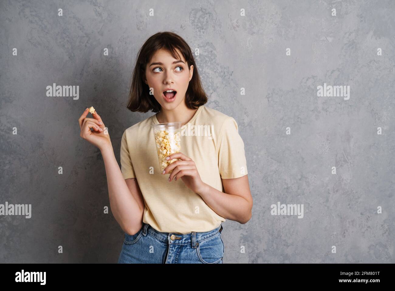 Excited shocked young girl eating popcorn while watching TV isolated ...