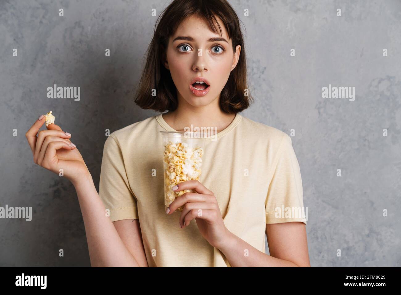 Excited shocked young girl eating popcorn while watching TV isolated ...