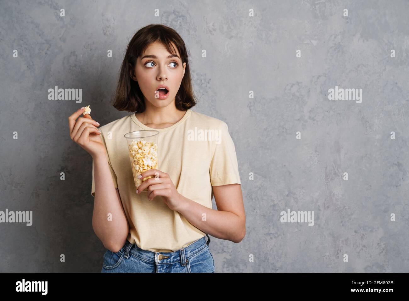 Excited shocked young girl eating popcorn while watching TV isolated ...
