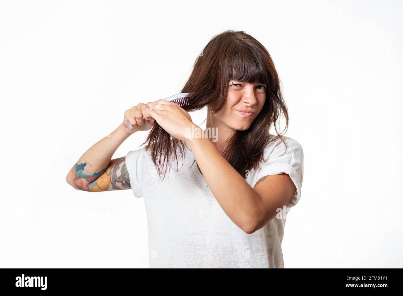 A young woman with tattoos combs a lock of hair, experiencing pain and ...