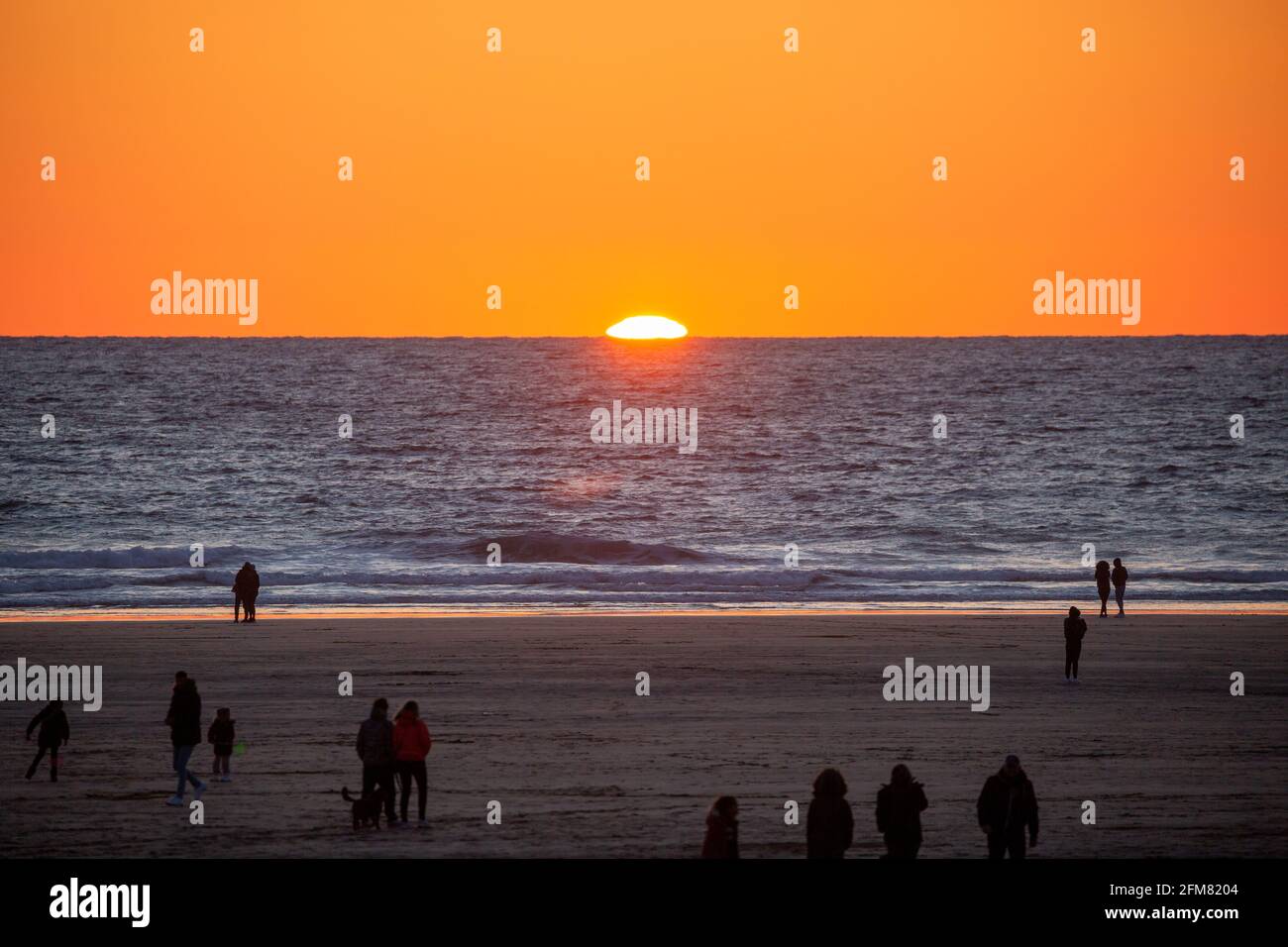 People stand on the beach to watch the Sunset over Perranporth Beach in ...
