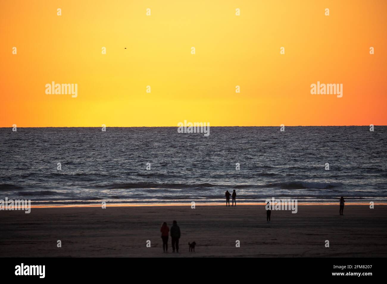 People stand on the beach to watch the Sunset over Perranporth Beach in ...