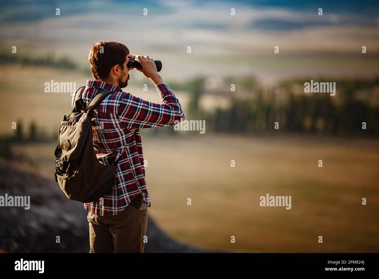 Guy looking at binoculars in hill. man in t-shirt with backpack. Young ...