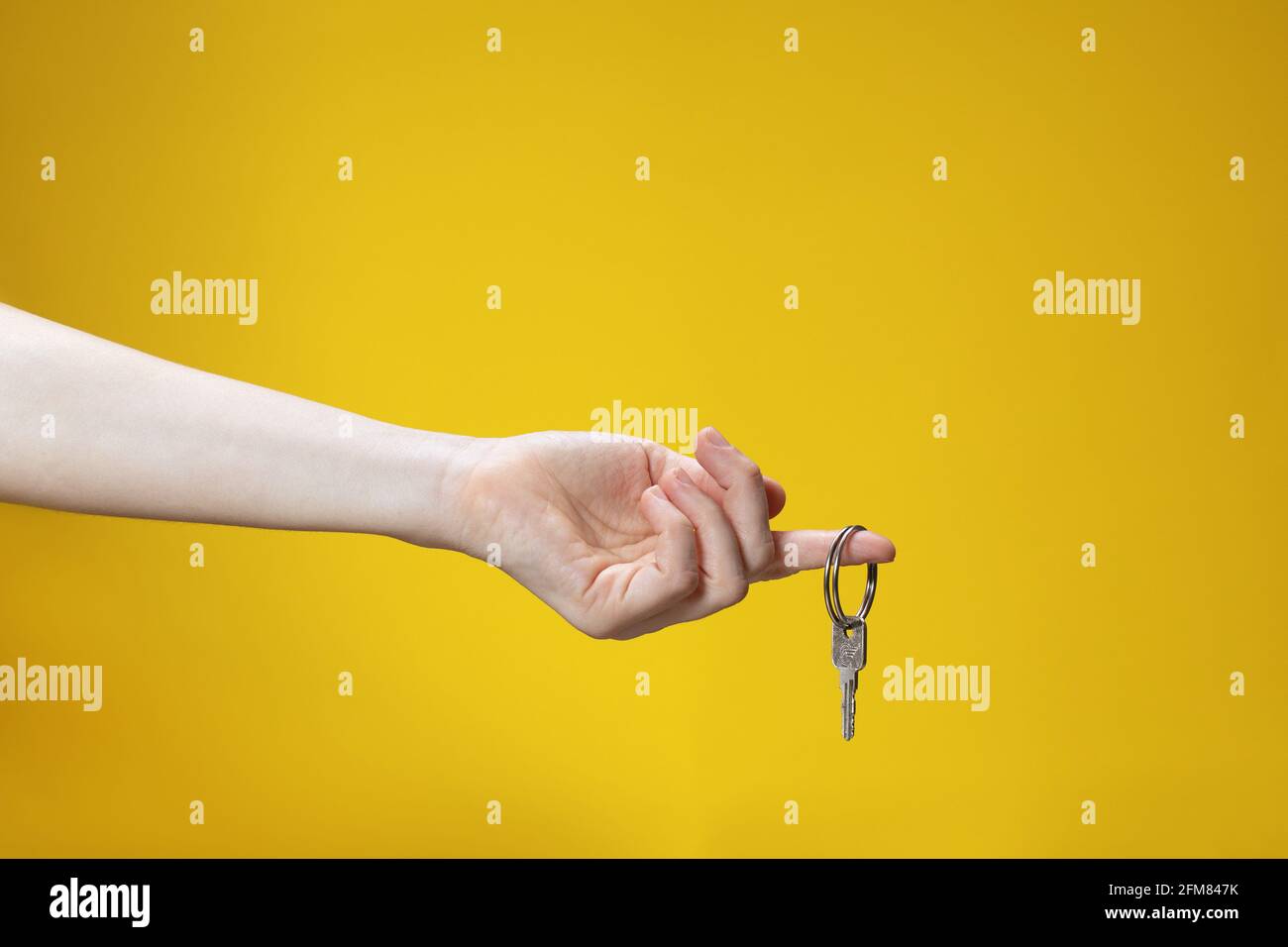 Outstretched woman hand with key on yellow background. Gives key to ...