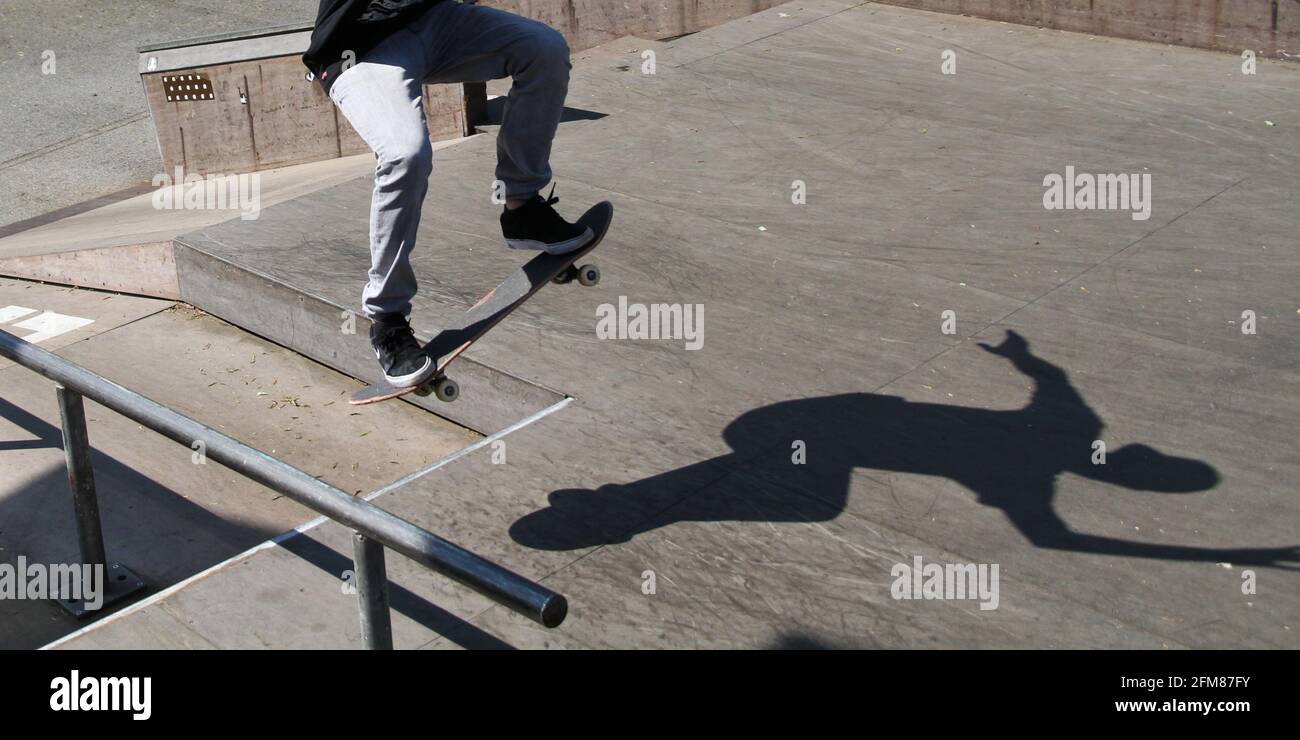 Detail of a young male and his shadow on the pavement performing a ...