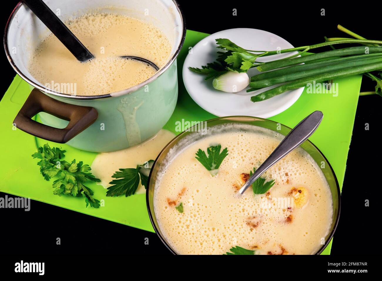 Dense creamy cauliflower soup in plate and pot, spilled soup on green ...