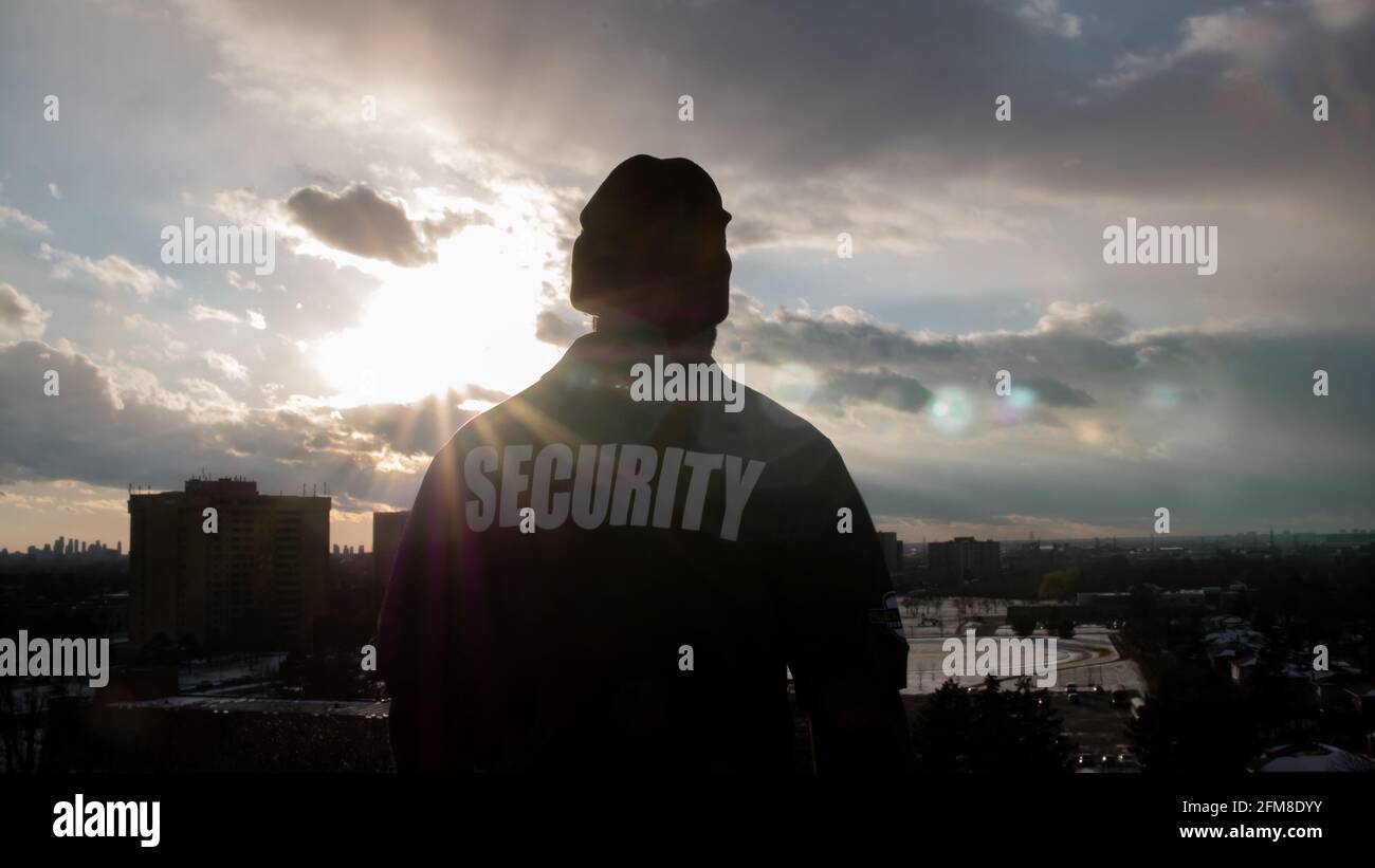 A rear view of a male security guard in uniform watching over the ...
