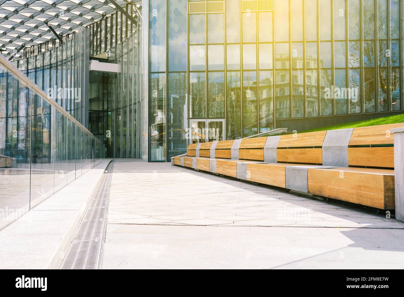 This is a modern glass building. Wooden bench and concrete walkway ...