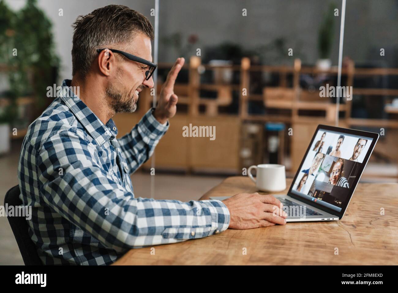 Happy grey man waving hand while taking conference call on laptop in ...