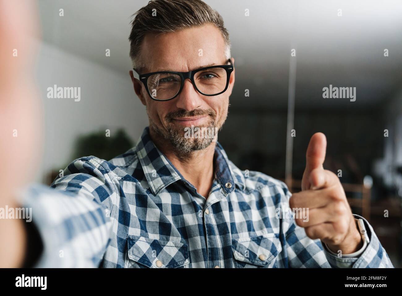 Happy white-haired man pointing finger at camera while taking selfie ...
