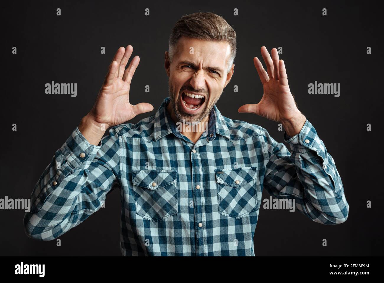 Furious unshaven man posing and screaming at camera isolated over black ...