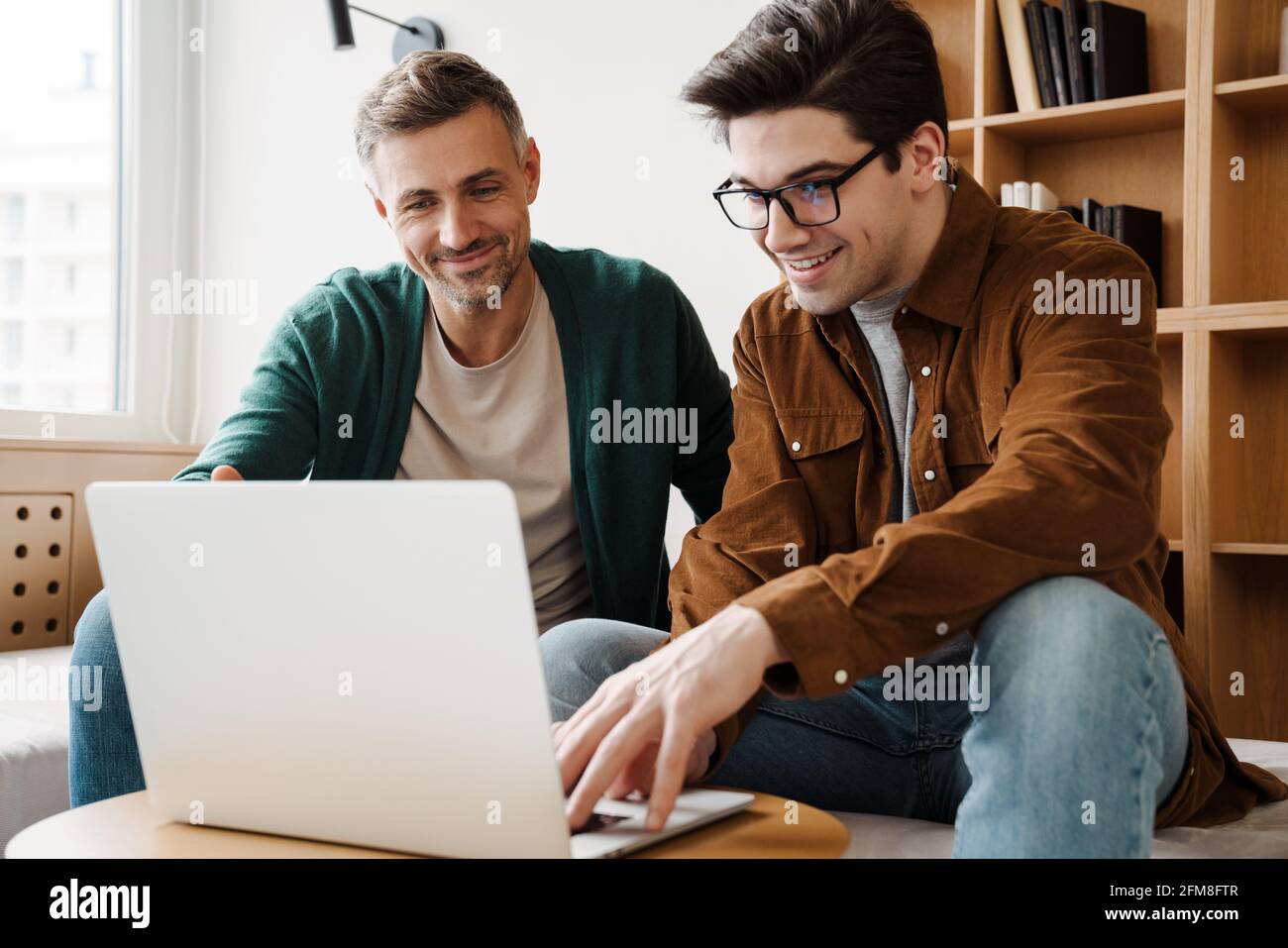 Happy young gay couple using laptop computer while sitting on a couch ...