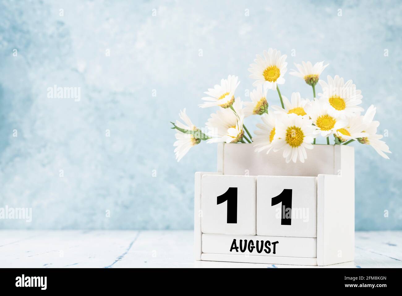 White cube calendar for August decorated with daisy flowers over blue ...