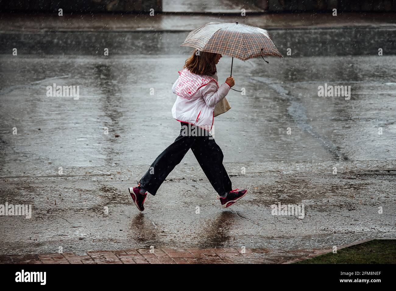 a girl with an umbrella runs through puddles in the rain. wet feet and ...