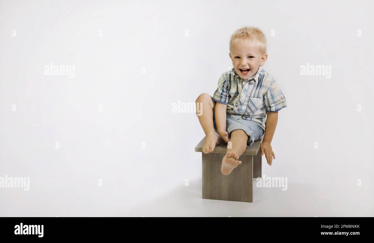 Cheerful little Caucasian boy sitting on a wooden chair isolated on ...