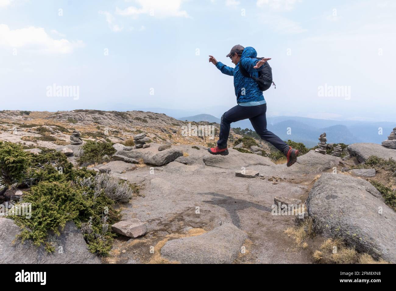 Hispanic hiker jumping up on mount Tlaloc under a cloudy sky in Mexico ...