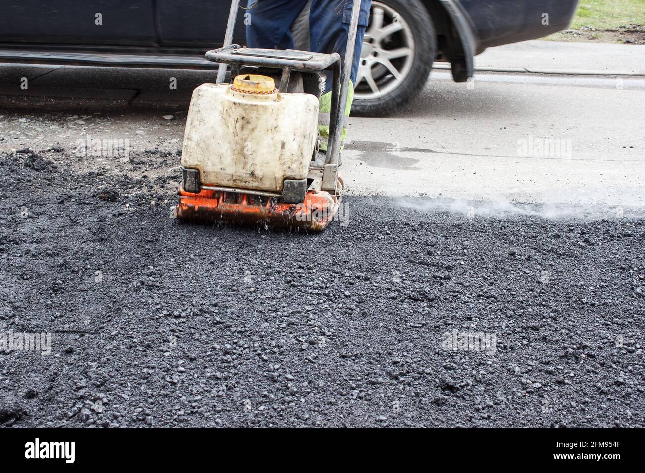 worker ramps the asphalt on the road with a mechanical rammer. laying ...