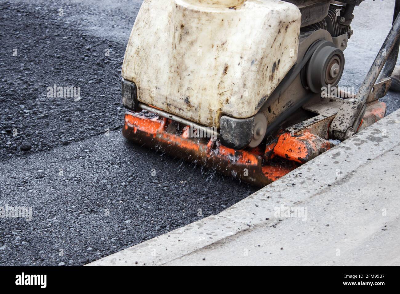 worker ramps the asphalt on the road with a mechanical rammer. laying ...