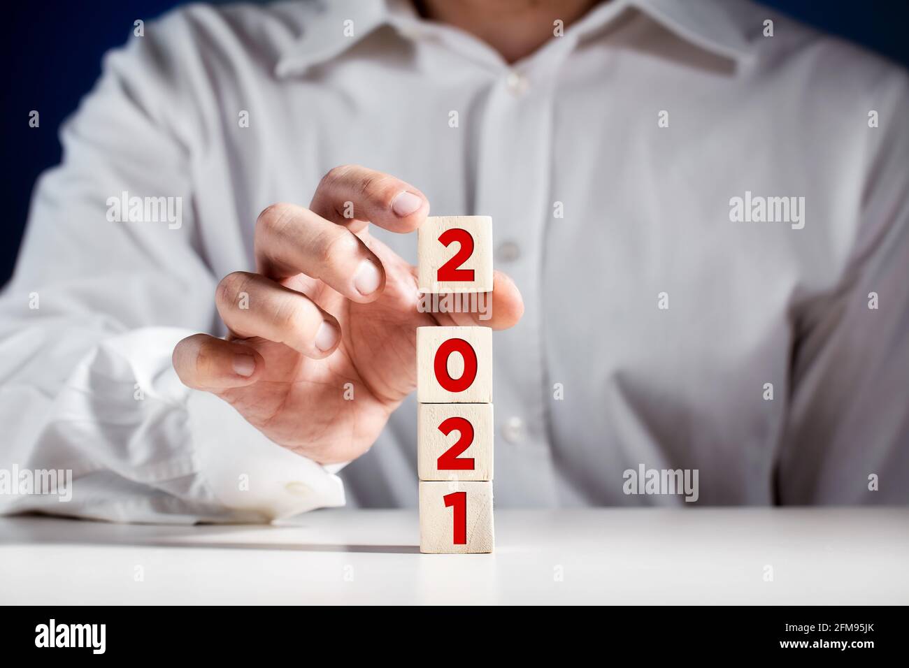 Businessman puts a cube on top of tiered wooden cubes with the year ...