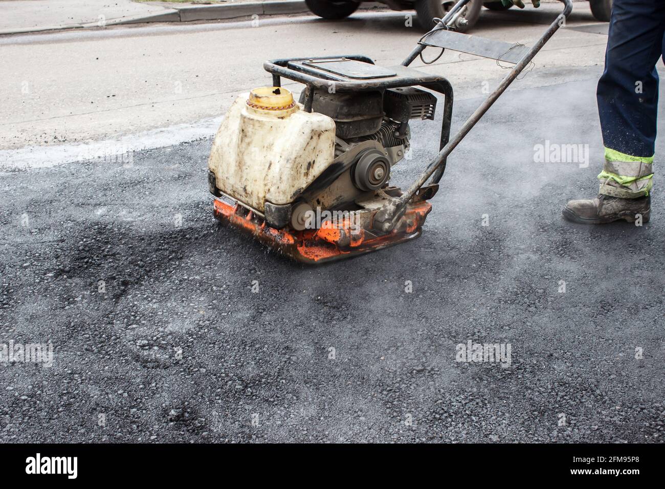 worker ramps the asphalt on the road with a mechanical rammer. laying ...