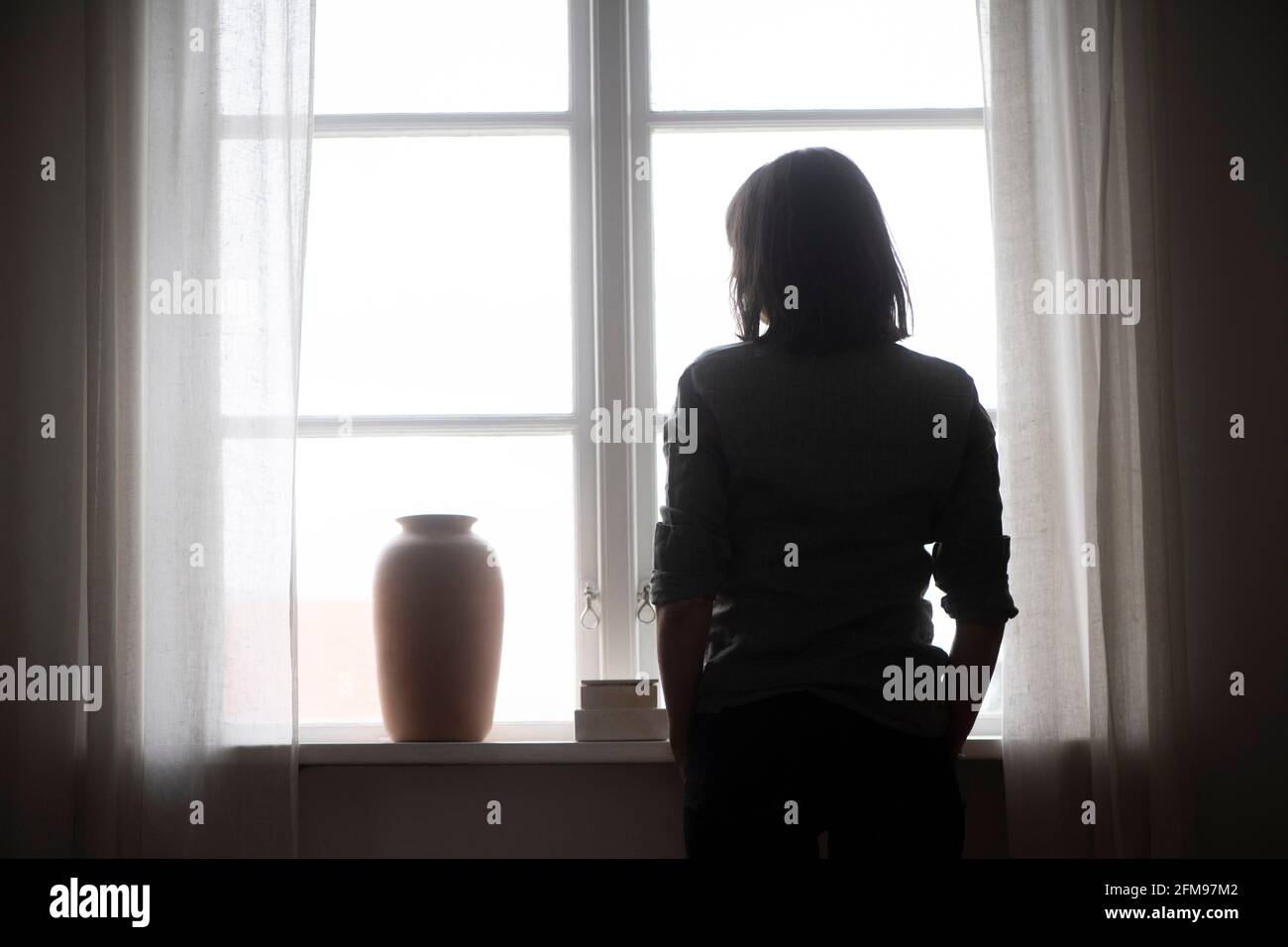 Domestic violence. A lonely sad, depressed, woman standing by a window ...