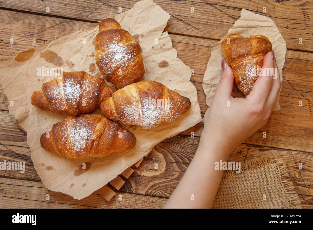 Hand taking french fresh crusty croissant from a wooden table top view ...