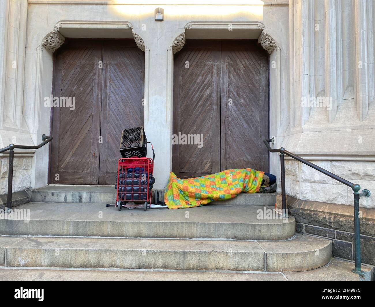 Homeless man with a colorful quilt sleeps up against the doors of a ...