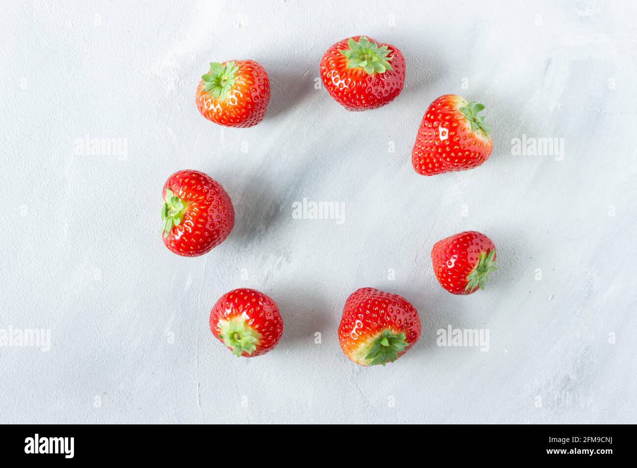 Perfectly red strawberries in a circle on gray textured background ...