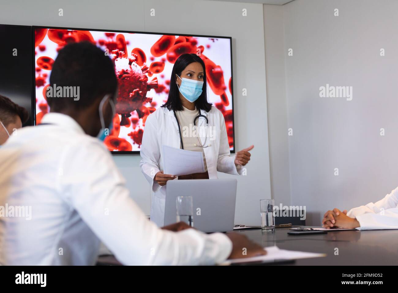Female doctor wearing face mask giving presentation to team of doctors ...