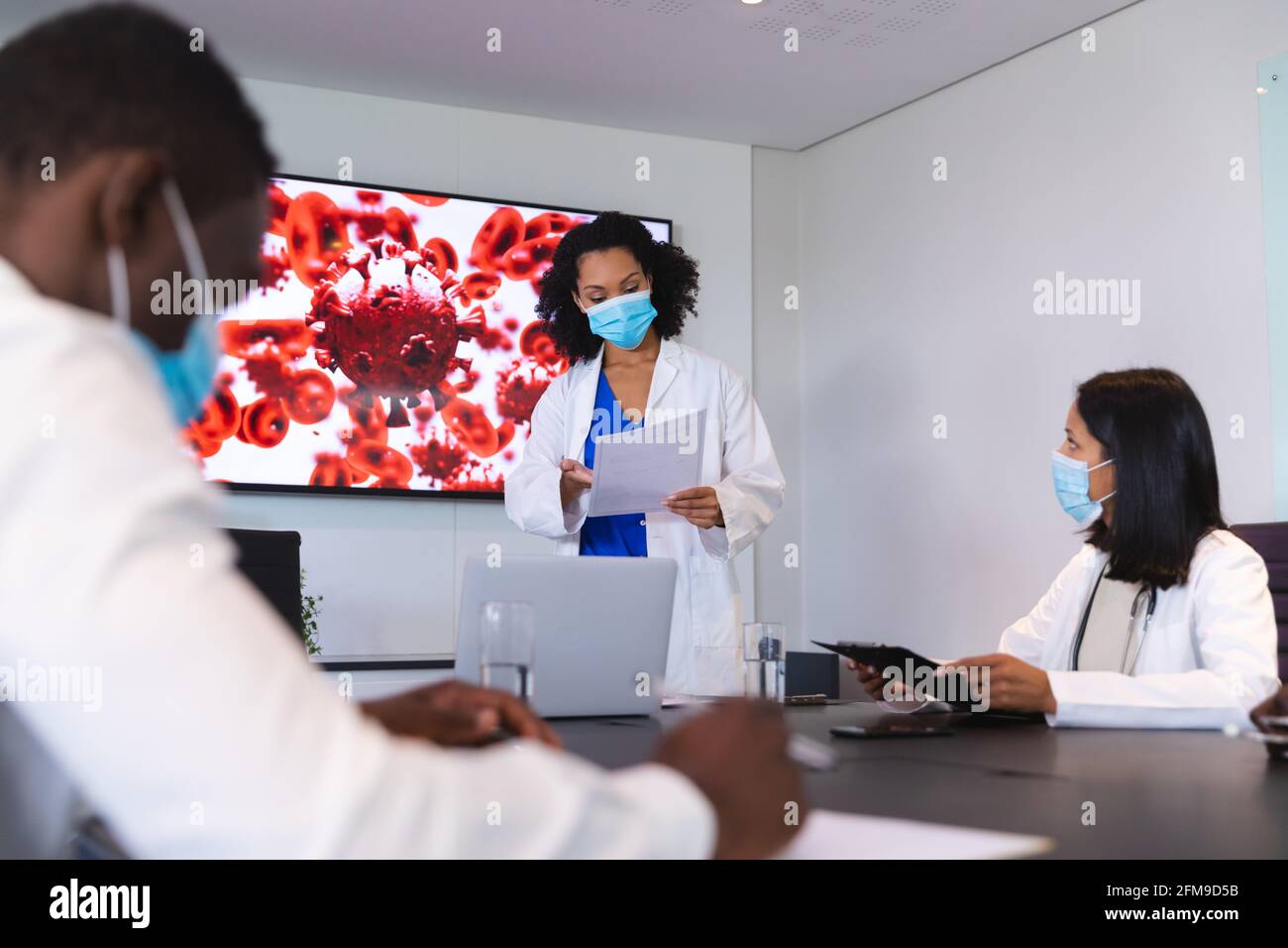 African american female doctor wearing face mask giving presentation to ...