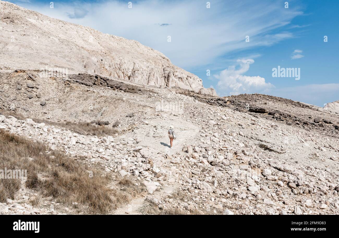 Rear view of tiny human walking on rocky path through arid terrain in ...