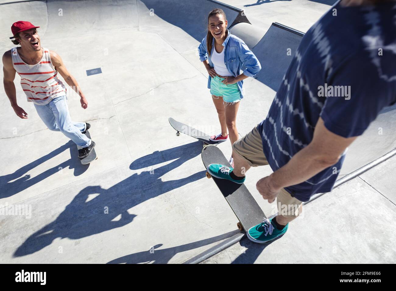 Three happy caucasian female and male friends skateboarding in the sun ...