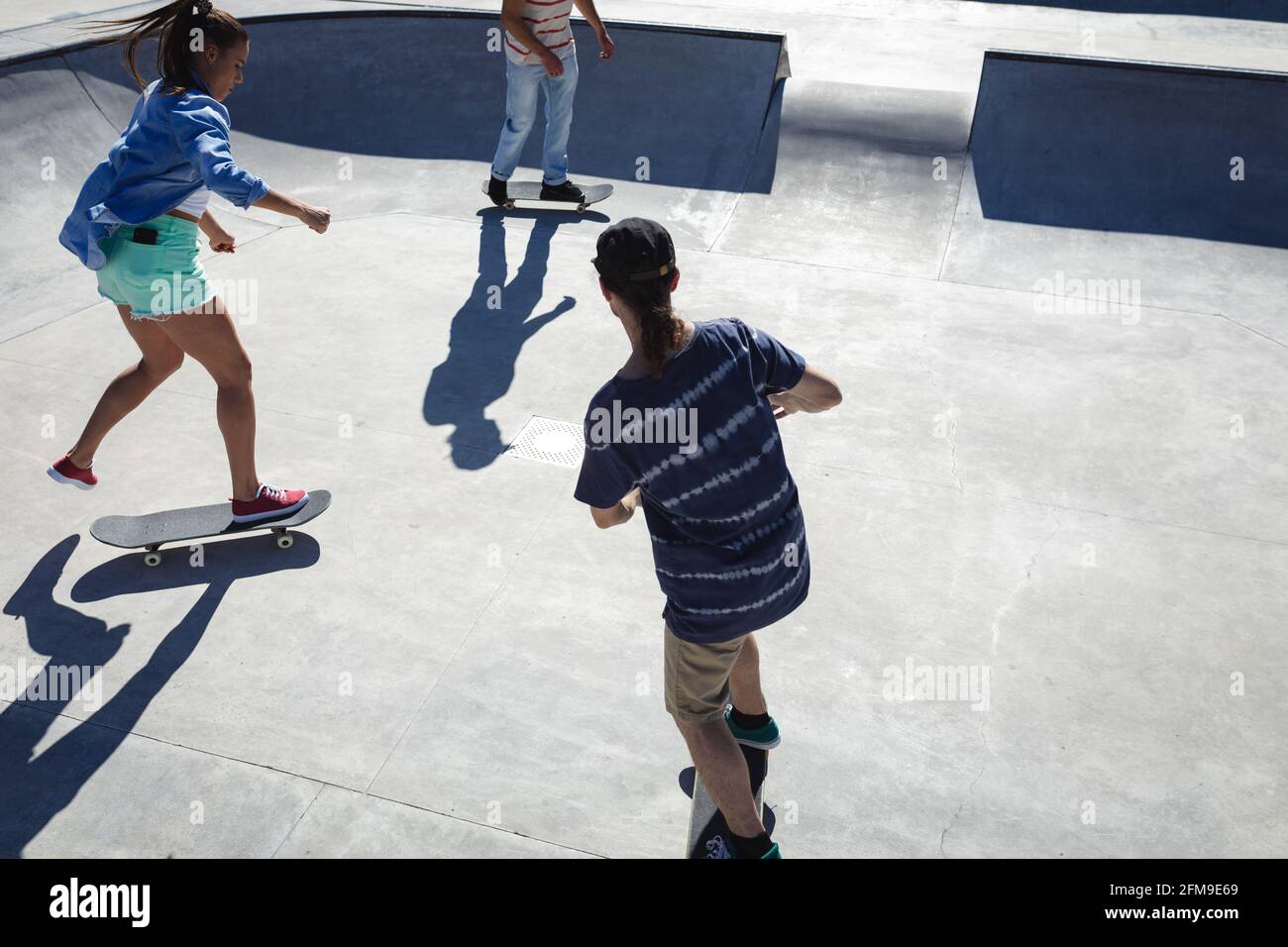 Three happy caucasian female and male friends skateboarding in the sun ...
